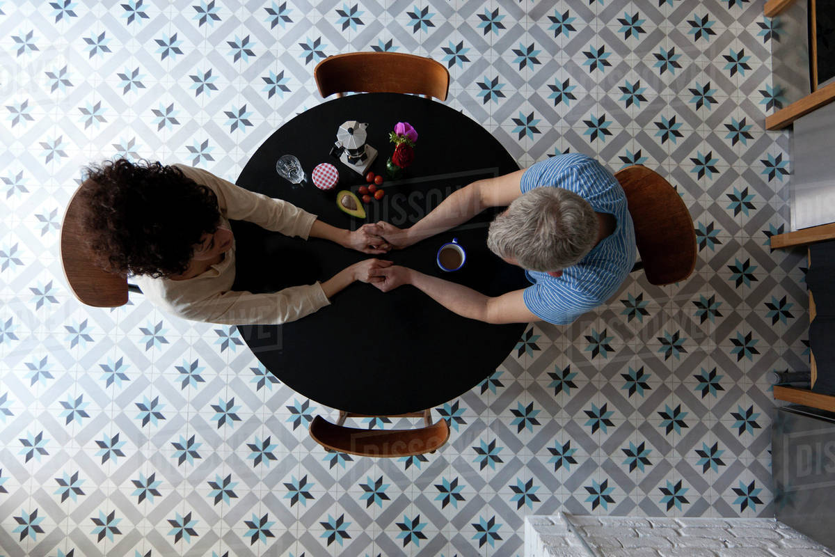 A mixed age couple holding hands at the breakfast table, directly above ...