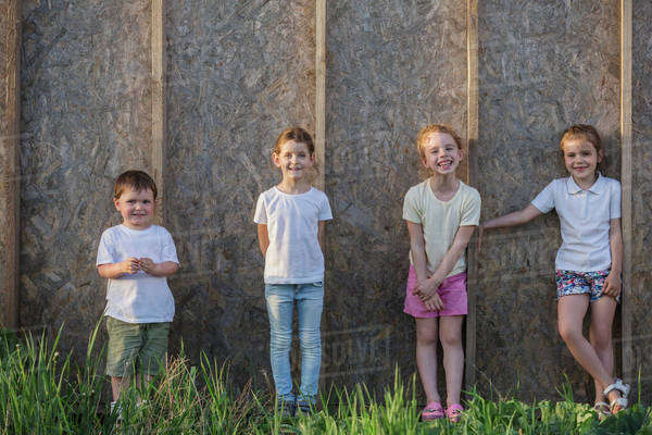 Portrait of cute children standing against wooden wall - Stock Photo ...