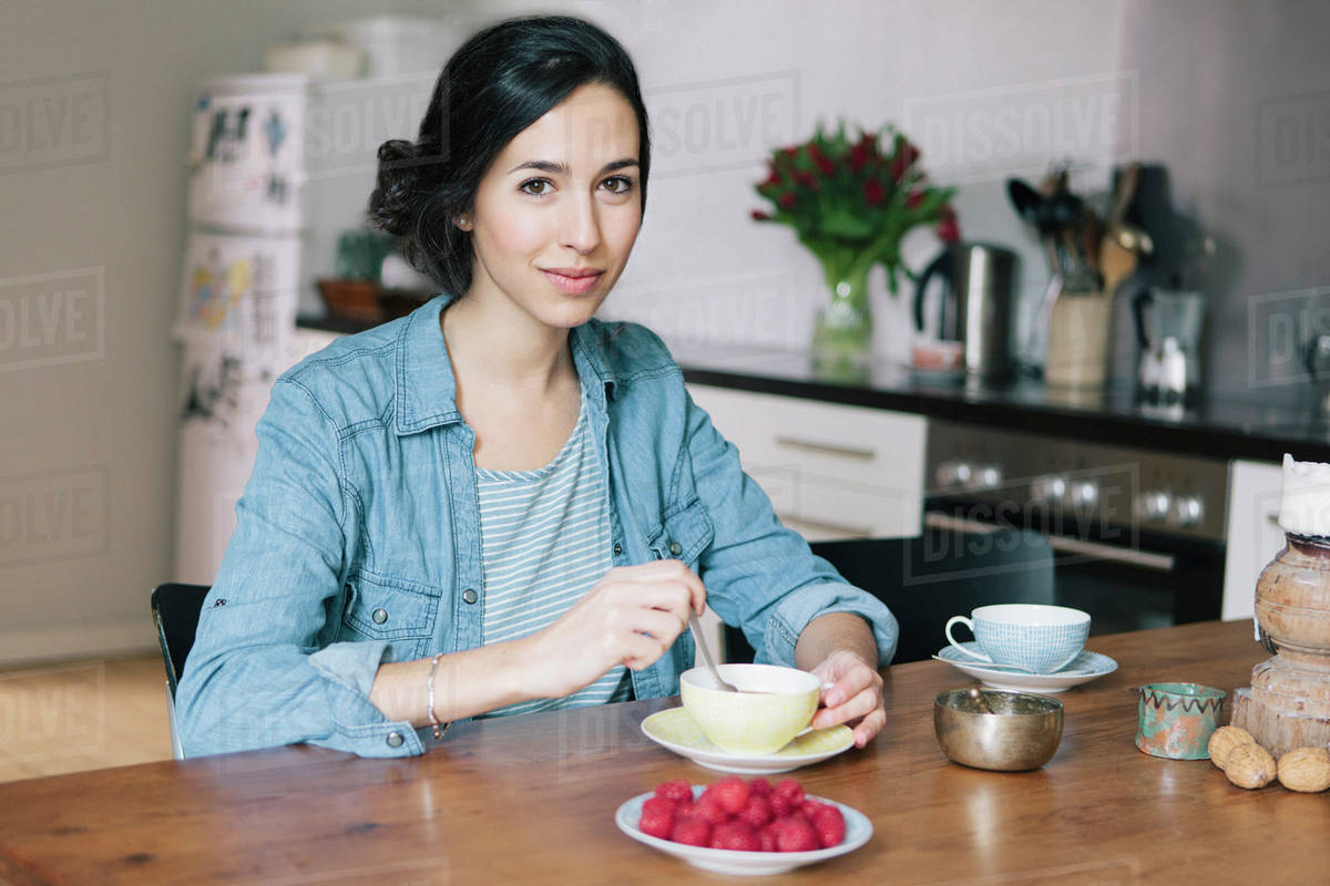 Portrait of happy young woman having coffee at table in kitchen - Stock ...