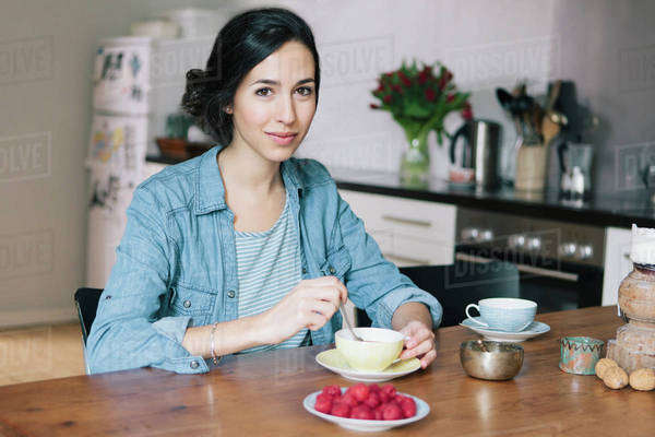 Portrait of happy young woman having coffee at table in kitchen - Stock ...