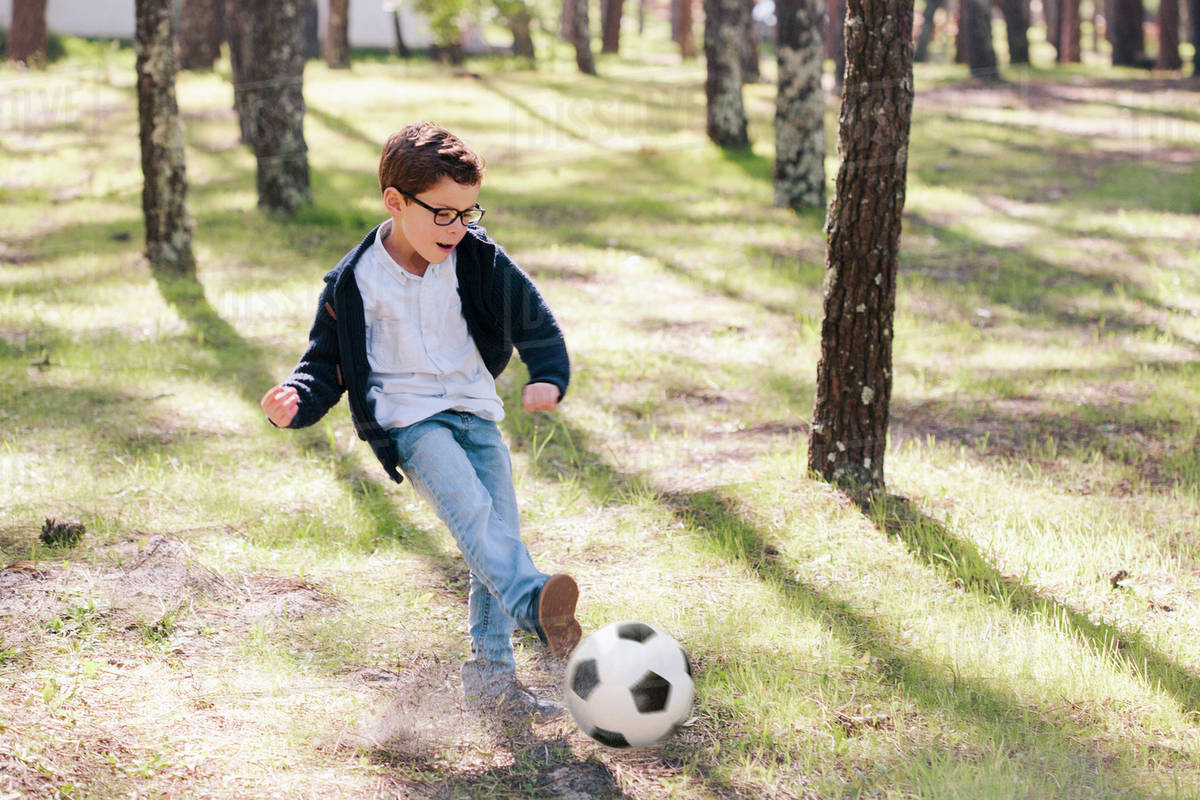 Full length of happy boy playing soccer in forest - Royalty-free Stock ...