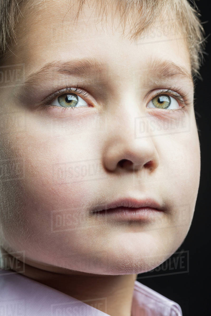 Close-up of thoughtful boy looking away against black background ...