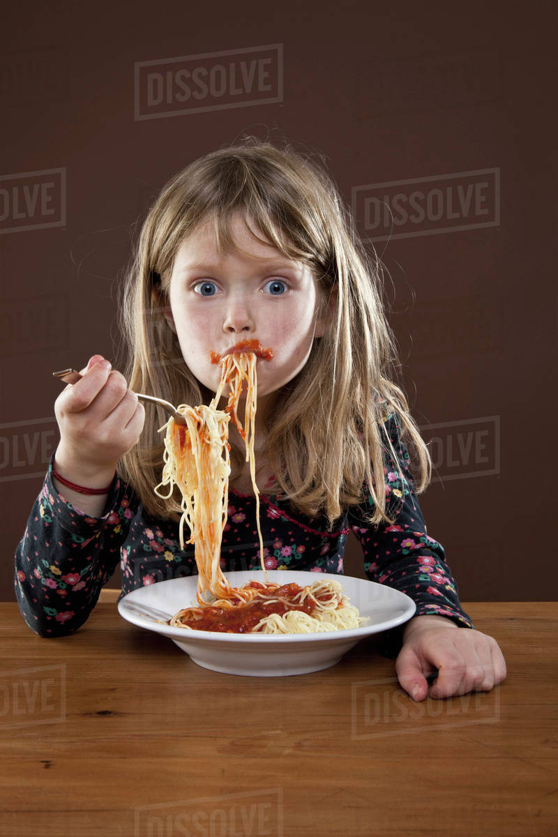 A young girl shoving spaghetti messily into her mouth, studio shot ...