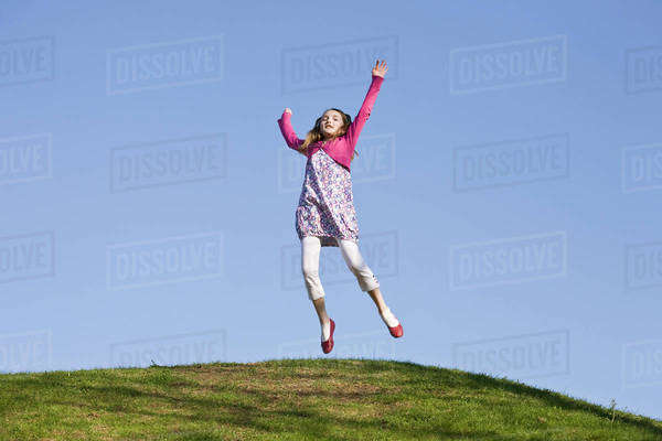 A girl jumping on a grass hill - Stock Photo - Dissolve