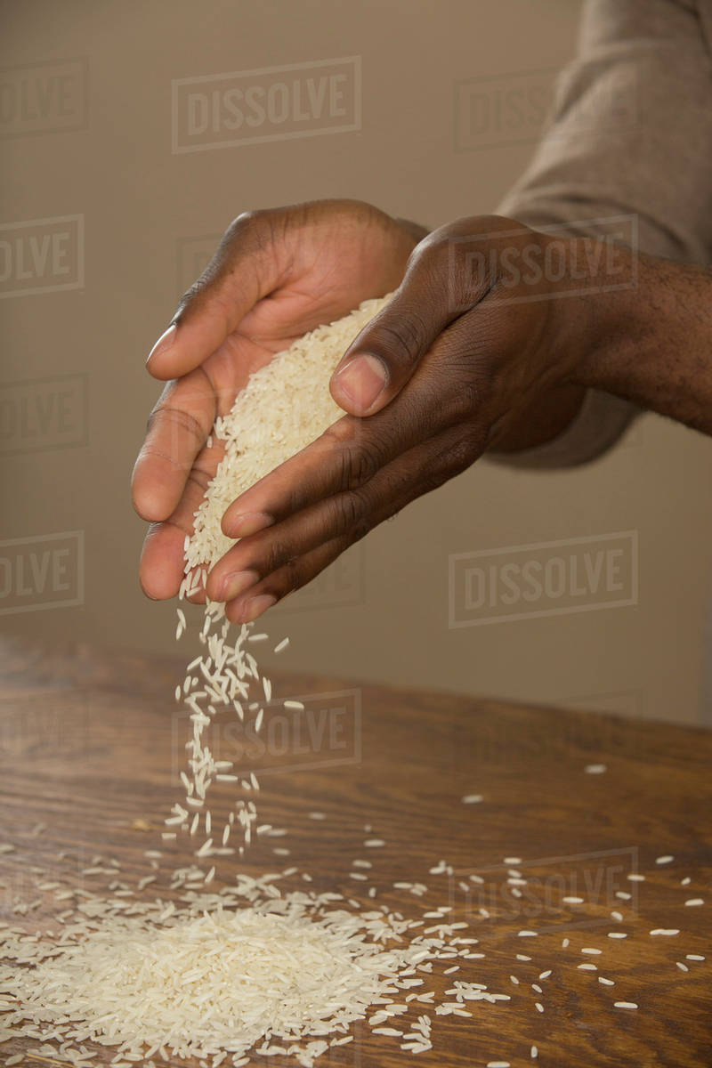 Hands pouring rice on table against colored background - Stock Photo ...