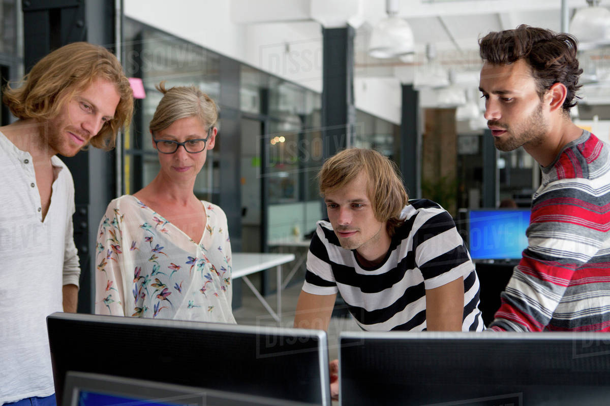 Office colleagues looking at computer in office - Stock Photo - Dissolve