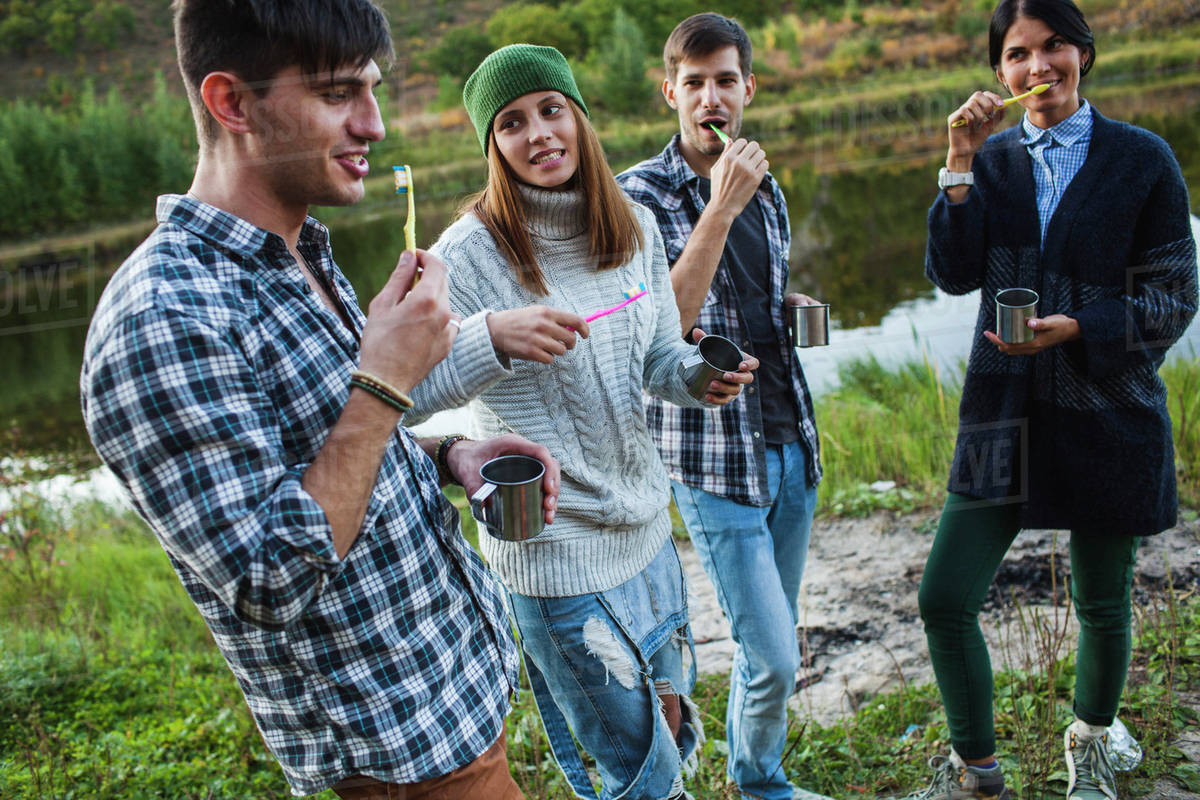 Friends brushing teeth at lakeshore in forest - Stock Photo - Dissolve