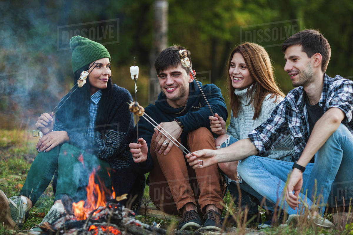 Smiling friends roasting marshmallows in forest - Royalty-free Stock ...