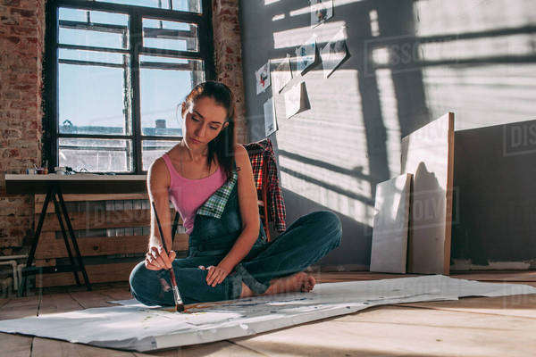 Woman painting while sitting on floor in art studio - Royalty-free ...