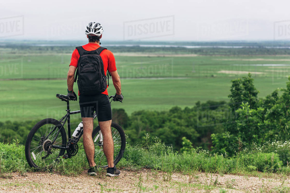 Rear view of man with mountain bike standing on hill - Royalty-free ...