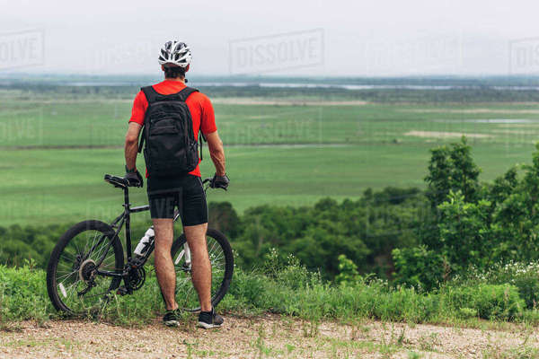 Rear view of man with mountain bike standing on hill - Royalty-free ...