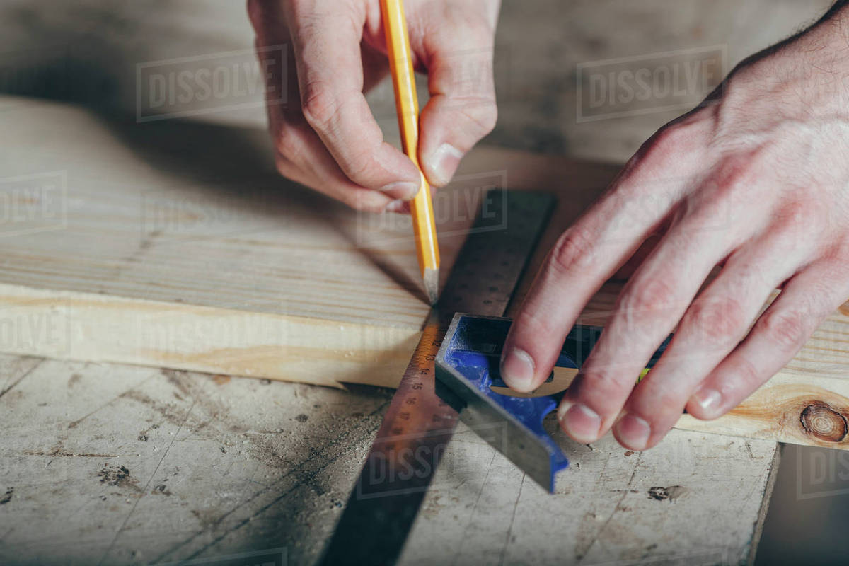 Cropped hands of carpenter marking on plank with pencil and ruler at ...