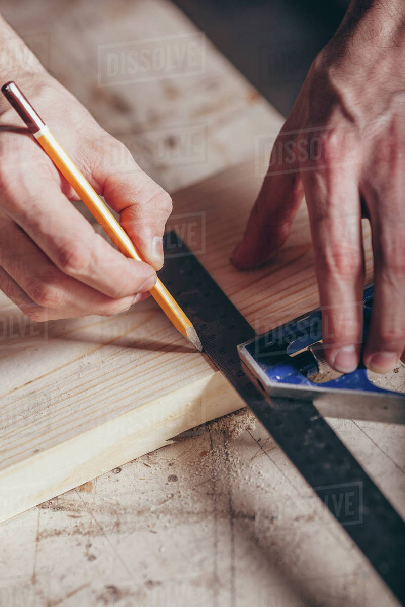 Cropped hands of carpenter marking on plank with pencil and ruler at ...