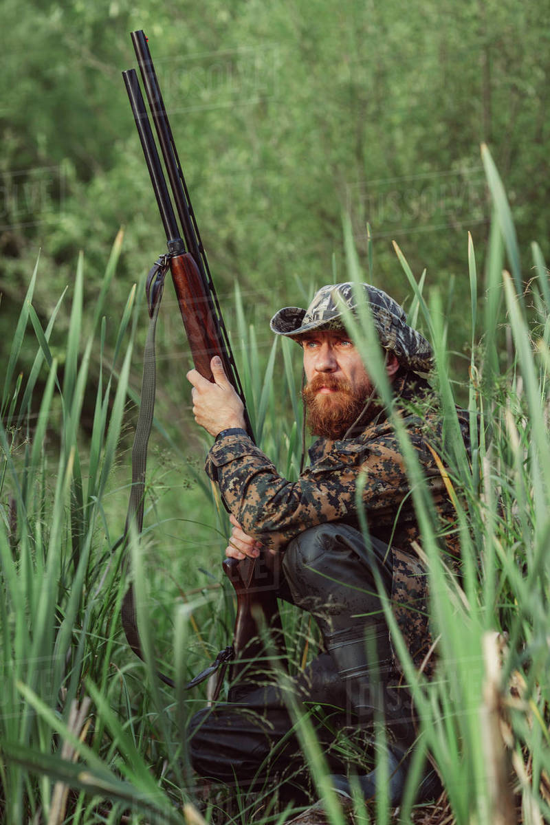 Hunter holding rifle while sitting on field - Stock Photo - Dissolve