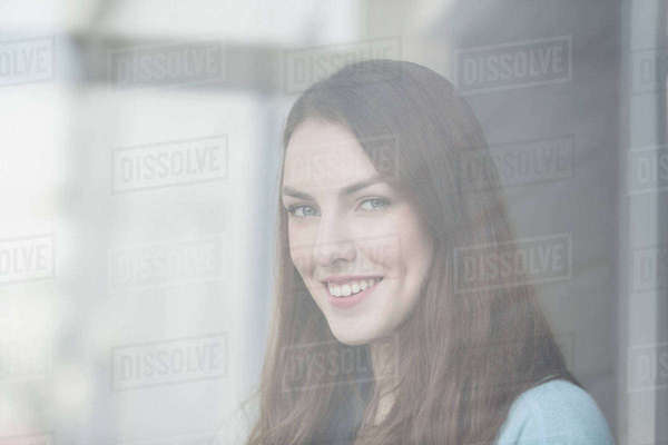 Portrait of smiling young beautiful woman seen through glass window ...