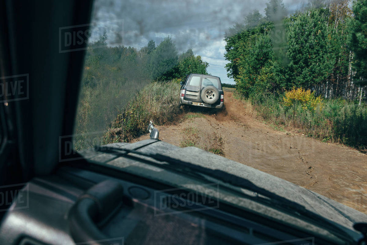 Off-road vehicle moving on dirt road amidst trees seen through ...