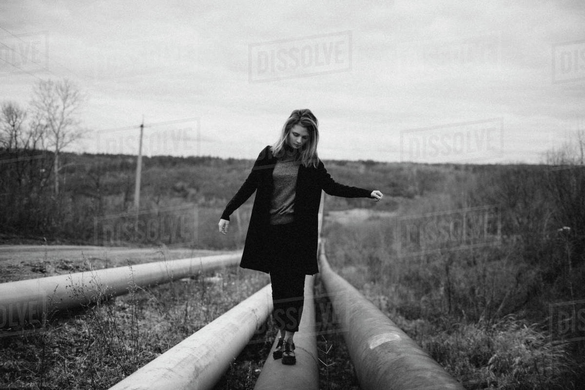 Full length of teenage girl walking on pipes over field against sky ...