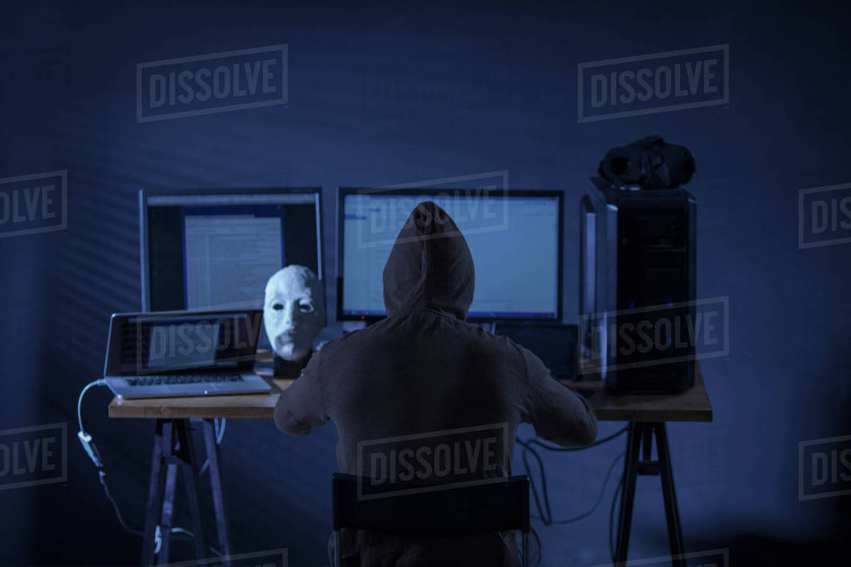 Rear view of computer hacker sitting at desk with equipment against ...