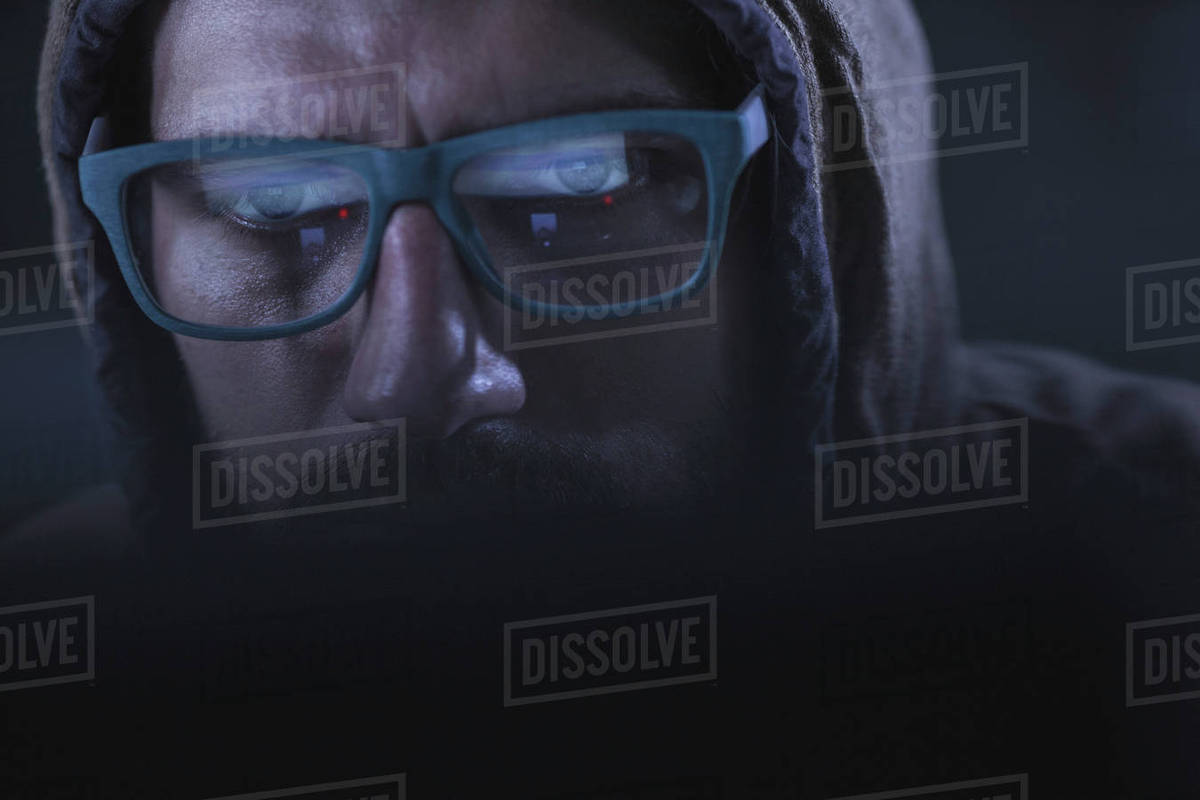 Close-up of serious computer hacker wearing eyeglasses and hood ...