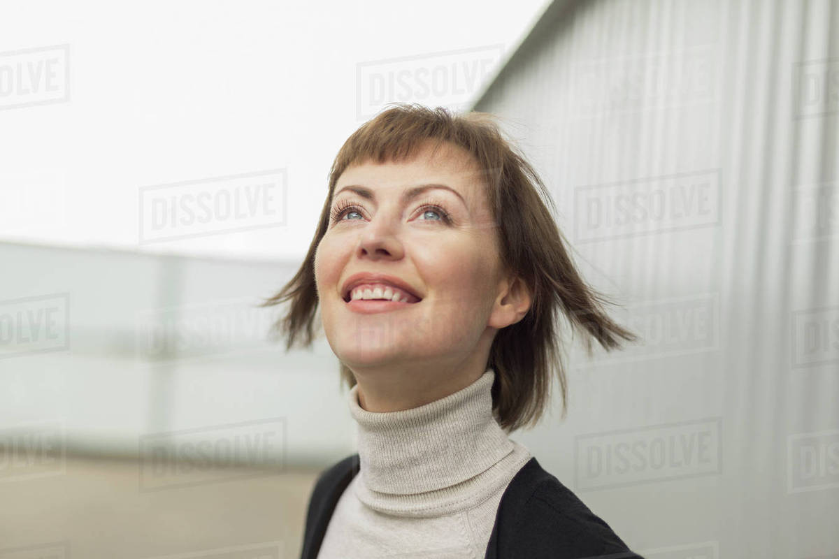 Low angle view of happy mid adult woman looking up against wall ...