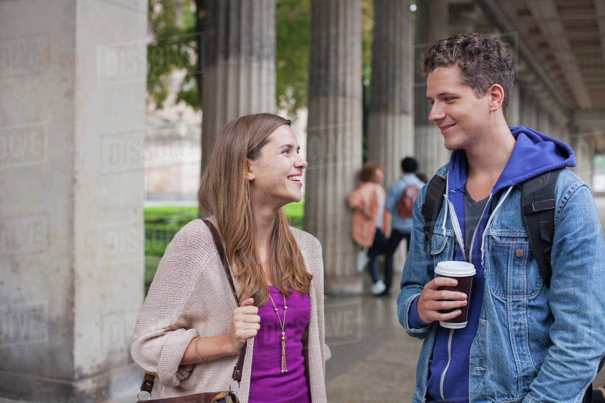 Smiling young friends talking while standing against columns - Stock ...