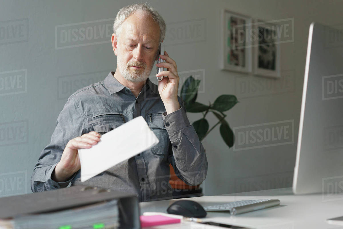 Businessman talking through mobile phone while working at desk in ...