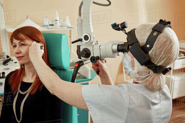 Doctor examining female patient's ear while using equipment at hospital ...
