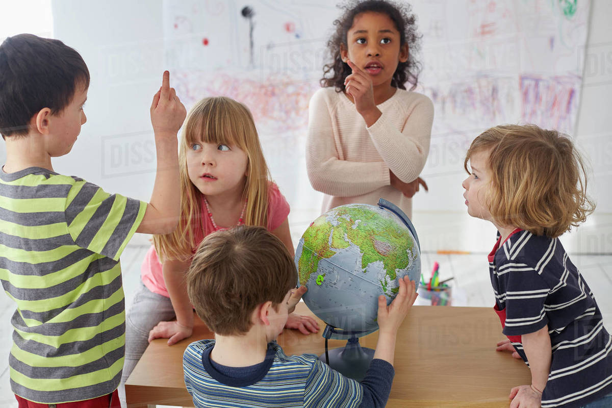 Children discussing while exploring globe at table in preschool ...