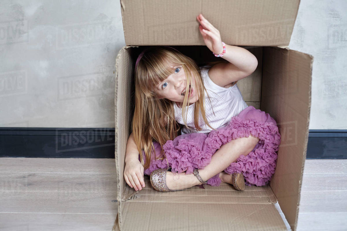 Portrait of playful girl sitting in box against wall - Royalty-free ...