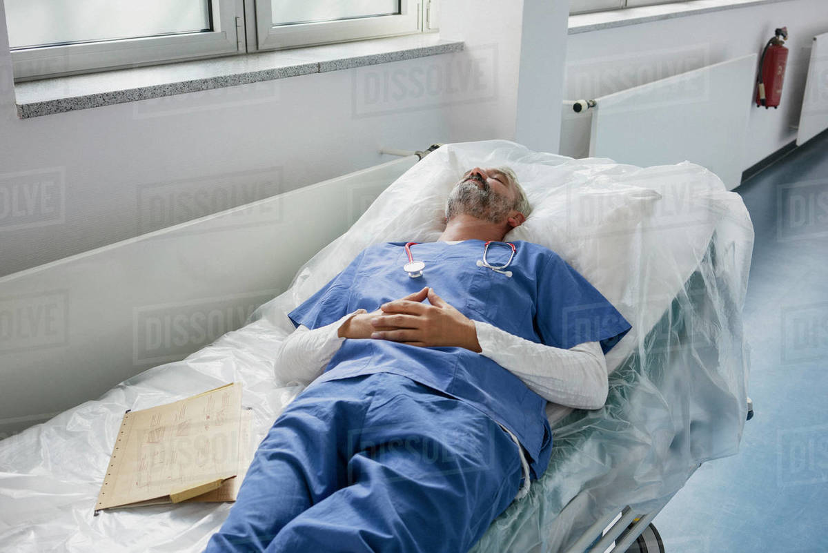 Exhausted doctor resting, sleeping on stretcher in hospital corridor ...