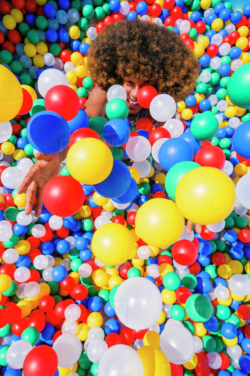 Playful young man throwing multicolor balls overhead in ball pool ...