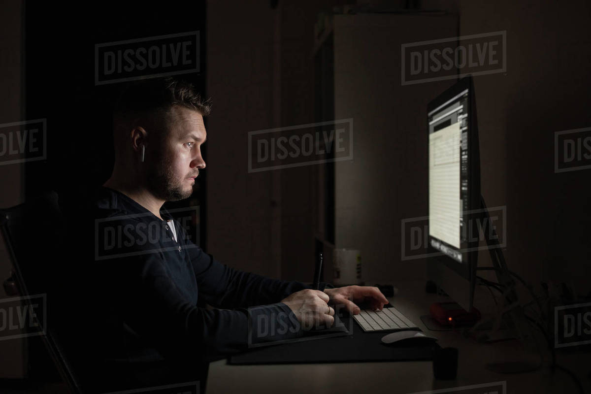 Man with earbuds working late at computer in dark room - Royalty-free ...