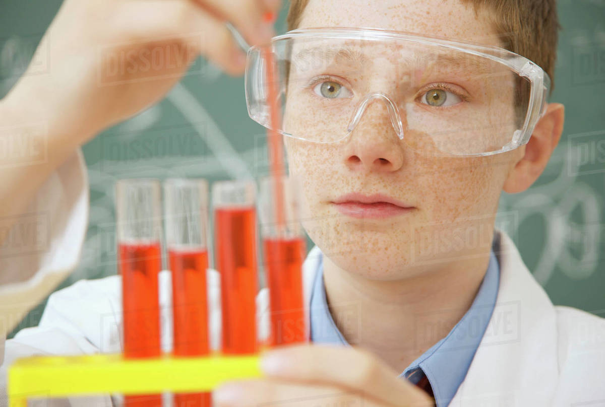 Curious junior high school boy examining liquid in science test tubes ...