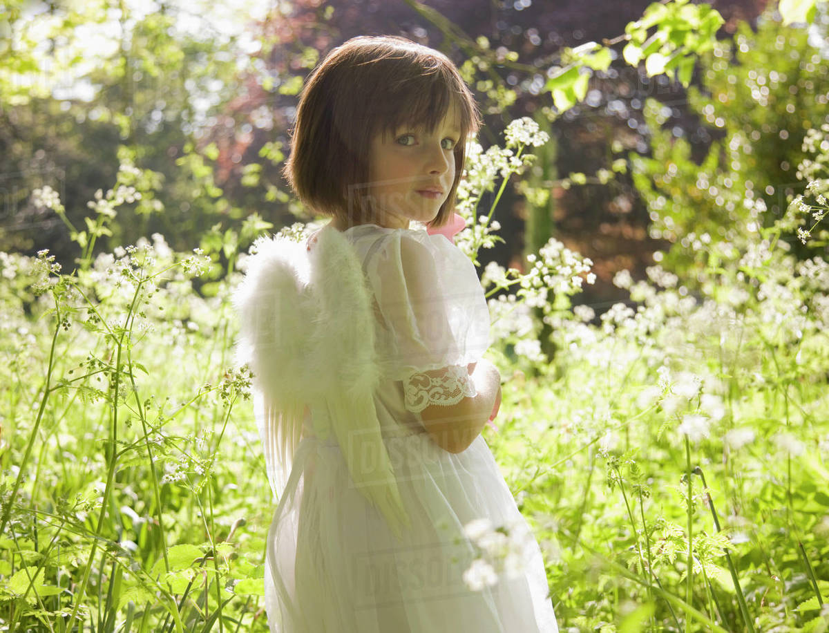 Portrait of young girl in a white fairy costume standing in a garden ...