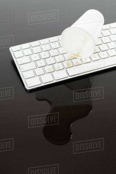 A cup of soda spilled on a computer keyboard - Stock Photo - Dissolve